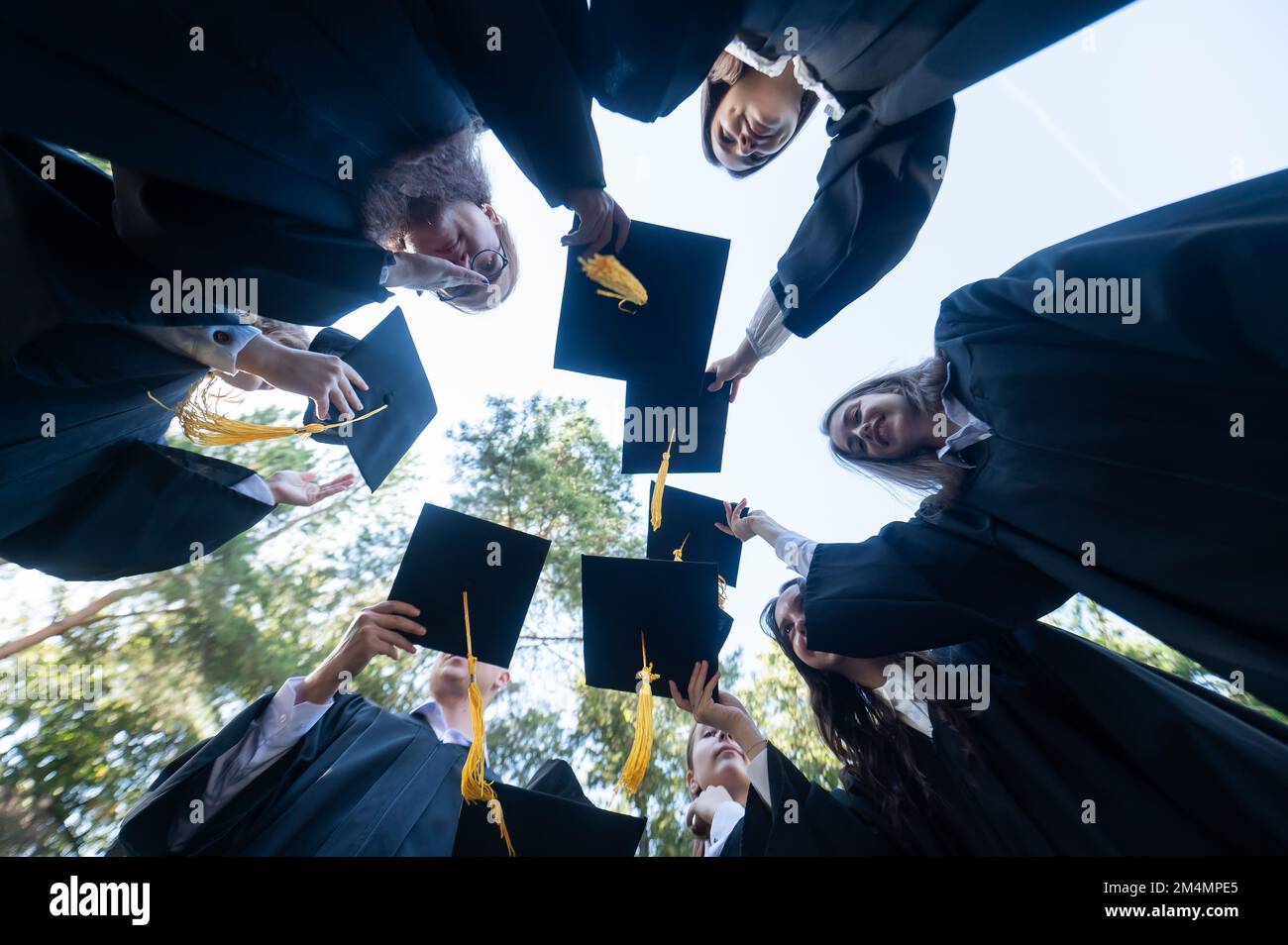 Classmates in graduation gowns toss their hats outdoors. Bottom view ...