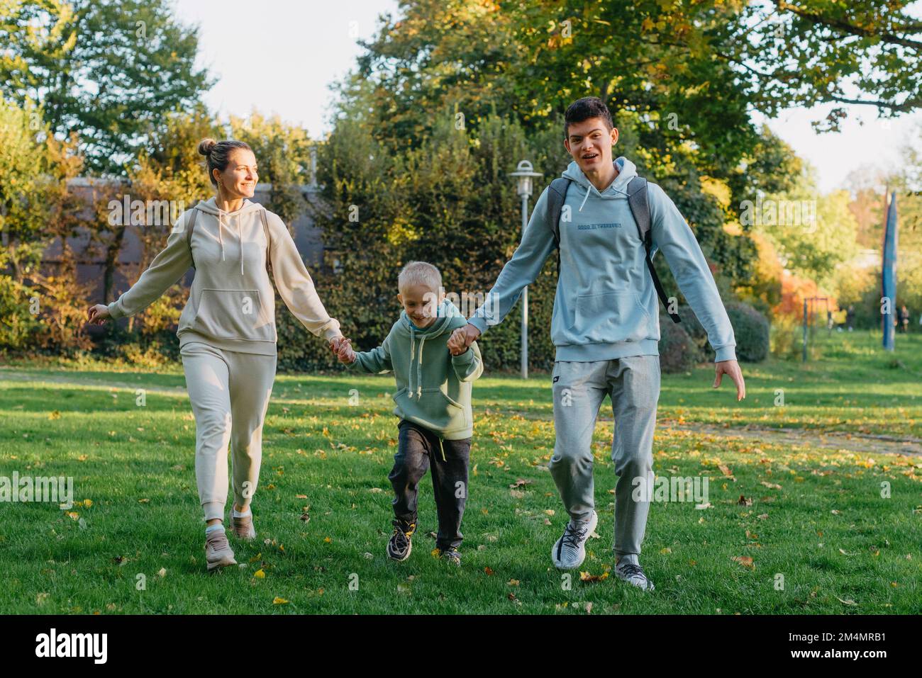 a family mom and 2 sons are having fun, running in the park and jumping ...