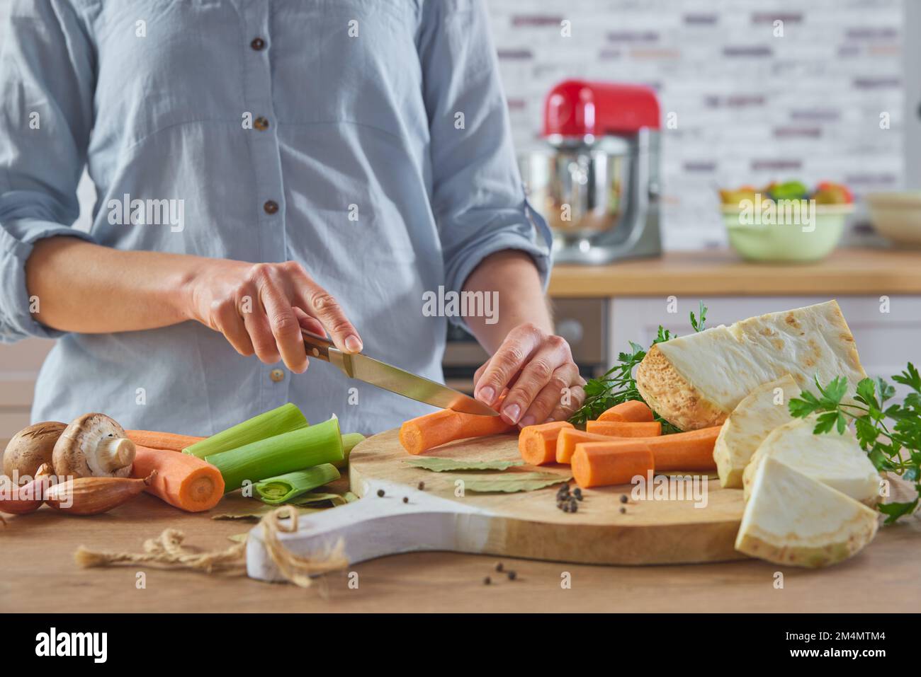 Crop unrecognizable female cutting fresh carrots with knife on wooden ...
