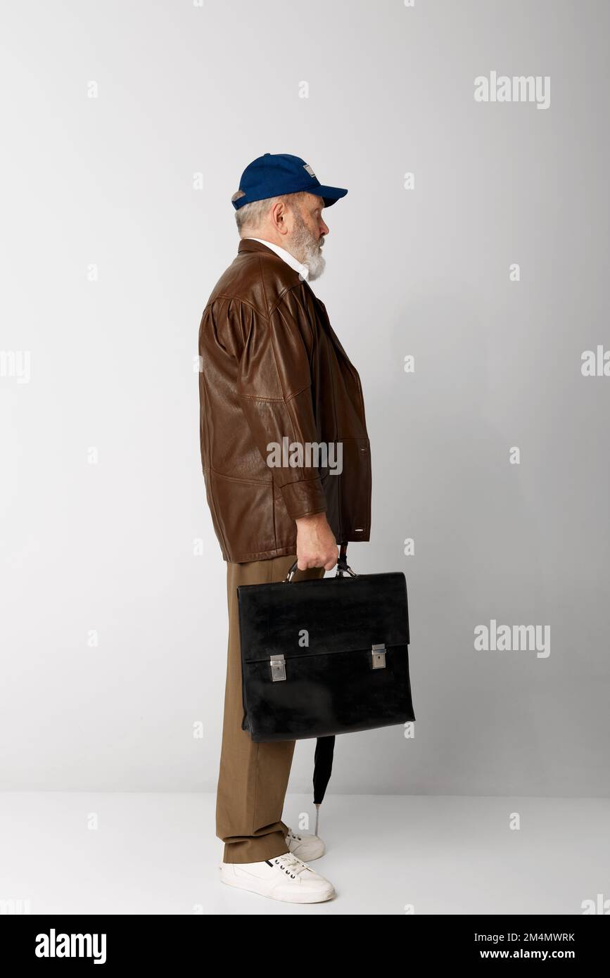 Portrait of senior old man in leather jacket posing with briefcase and ...