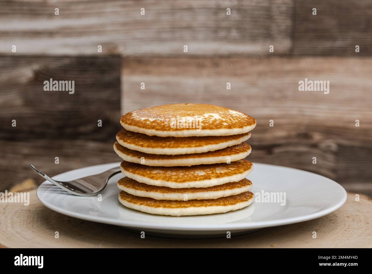 A large plate stack of pancakes with a fork against a wood background ...