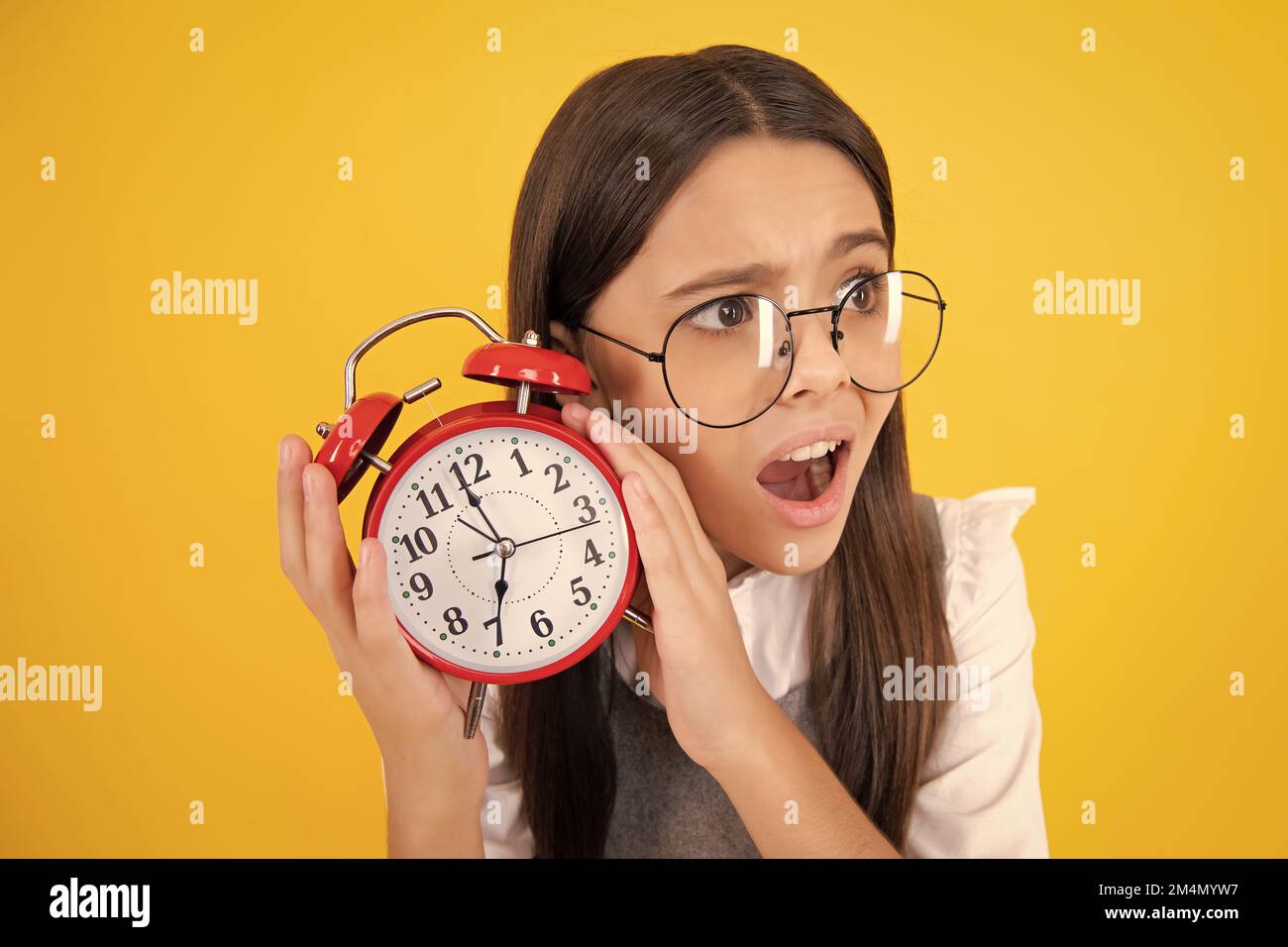 Surprised funny teenager girl child hold clock isolated on yellow ...
