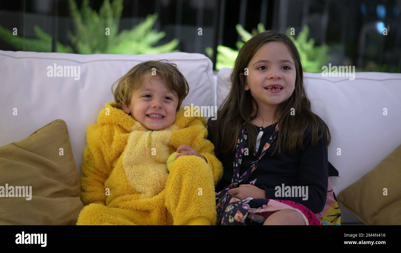 Cute little brother and sister sitting on sofa at living room smiling ...