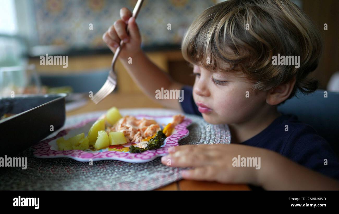 Little boy eating food at lunch table. Small child eats healthy organic ...