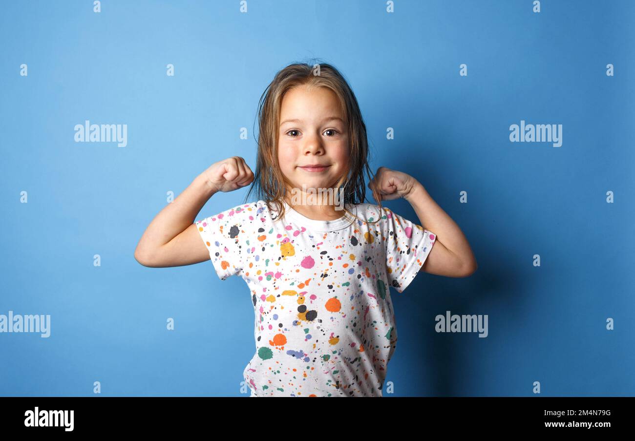 a little girl shows the strength of her biceps by raising her arms up ...