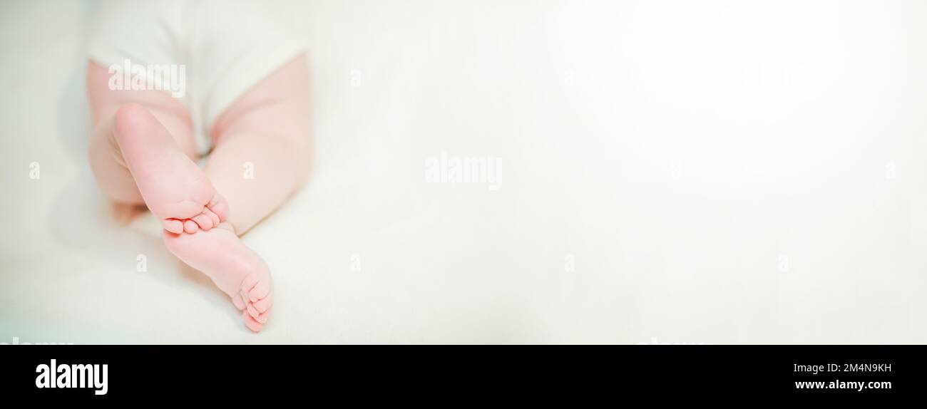 Crossed legs of the baby on a white background. A little girl lies on a ...