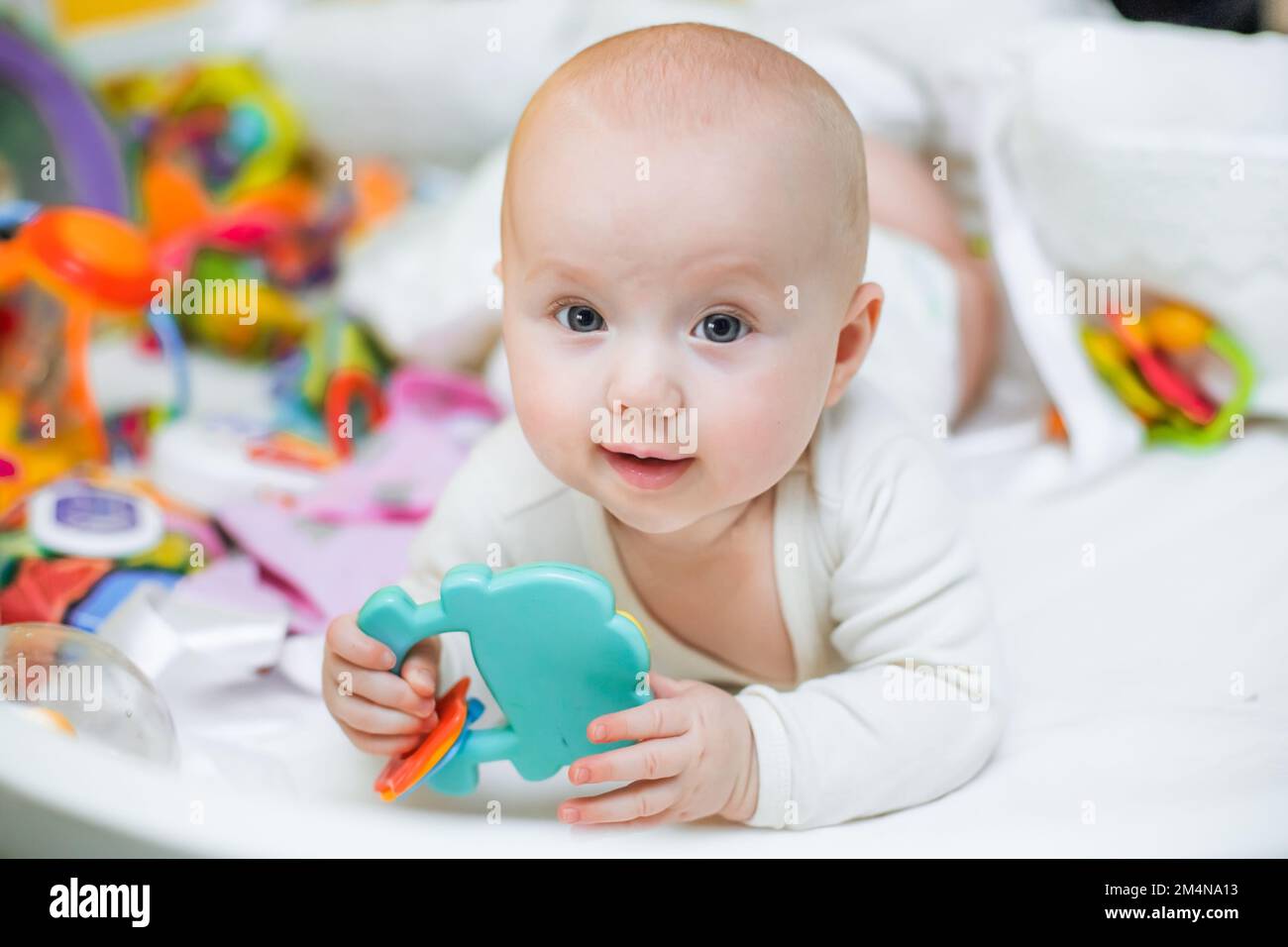 A funny baby in white clothes lies on a cot near toys. A cute little newborn girl lies on a bed ...
