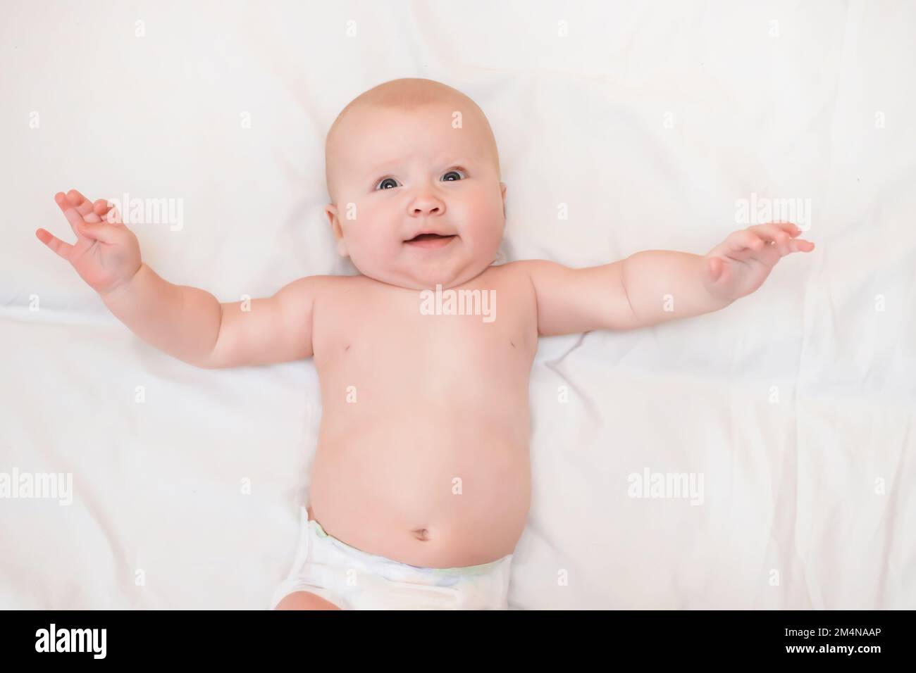 A smiling baby on a white bed. Infant baby girl spreading arms in ...