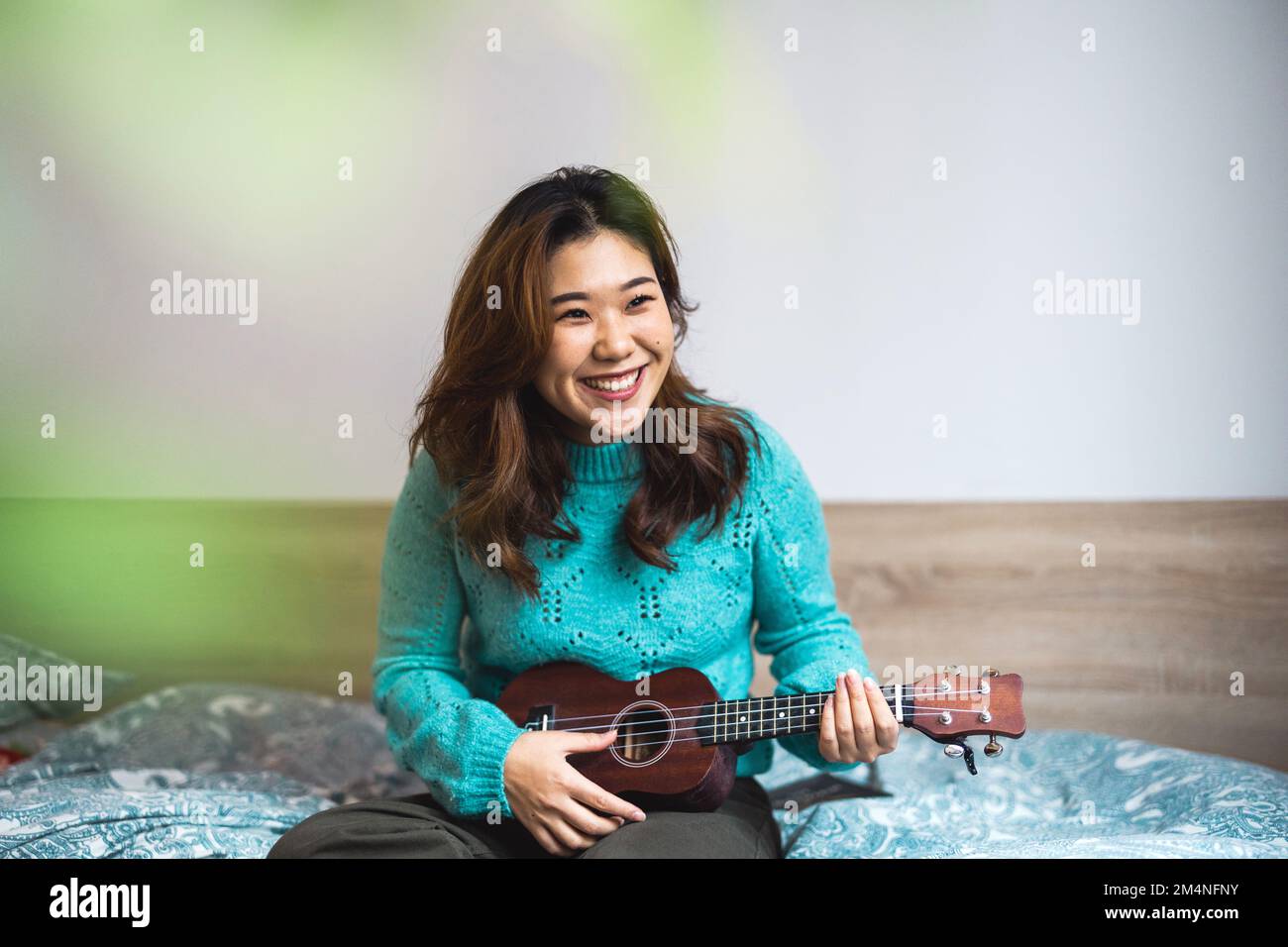 Young woman having fun playing Ukulele in her studio apartment Stock ...