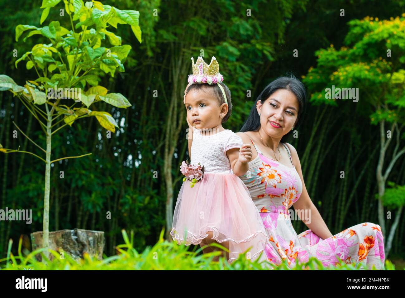 latina mother teaching her little brown baby to walk, sitting in a park ...