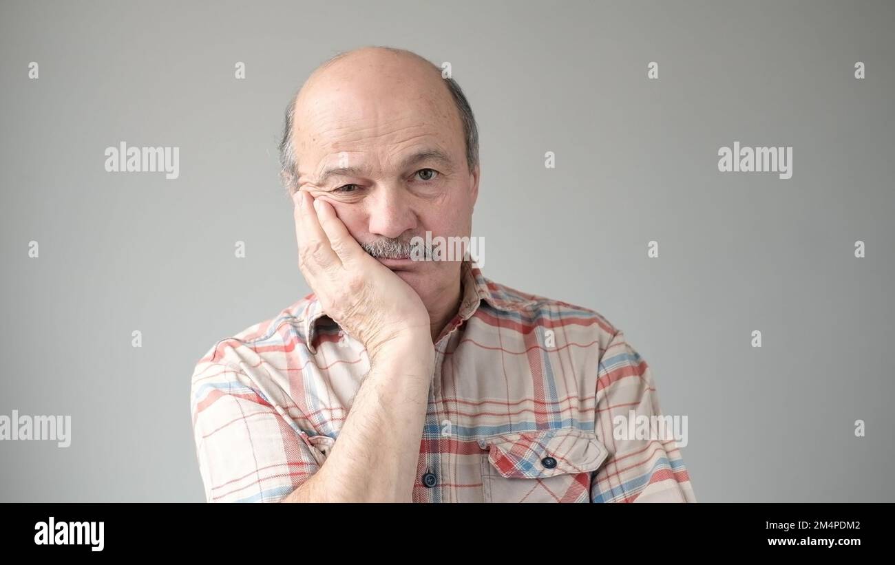 Very bored senior adult man holding hand on cheek , looking tired and ...