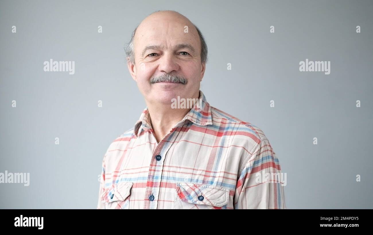 Portrait of smiling positive mature man standing on gray background ...