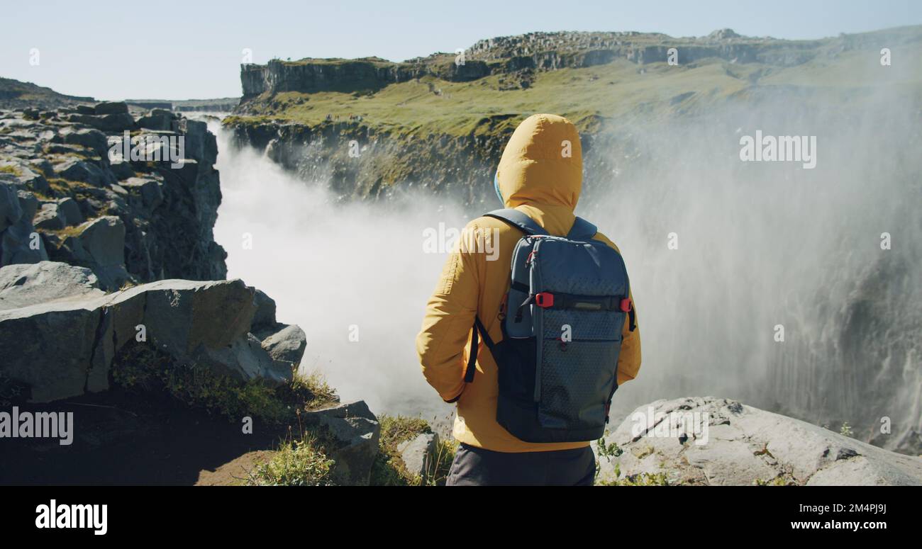 Man in yellow jacket and backpack walking on cliff edge enjoying ...