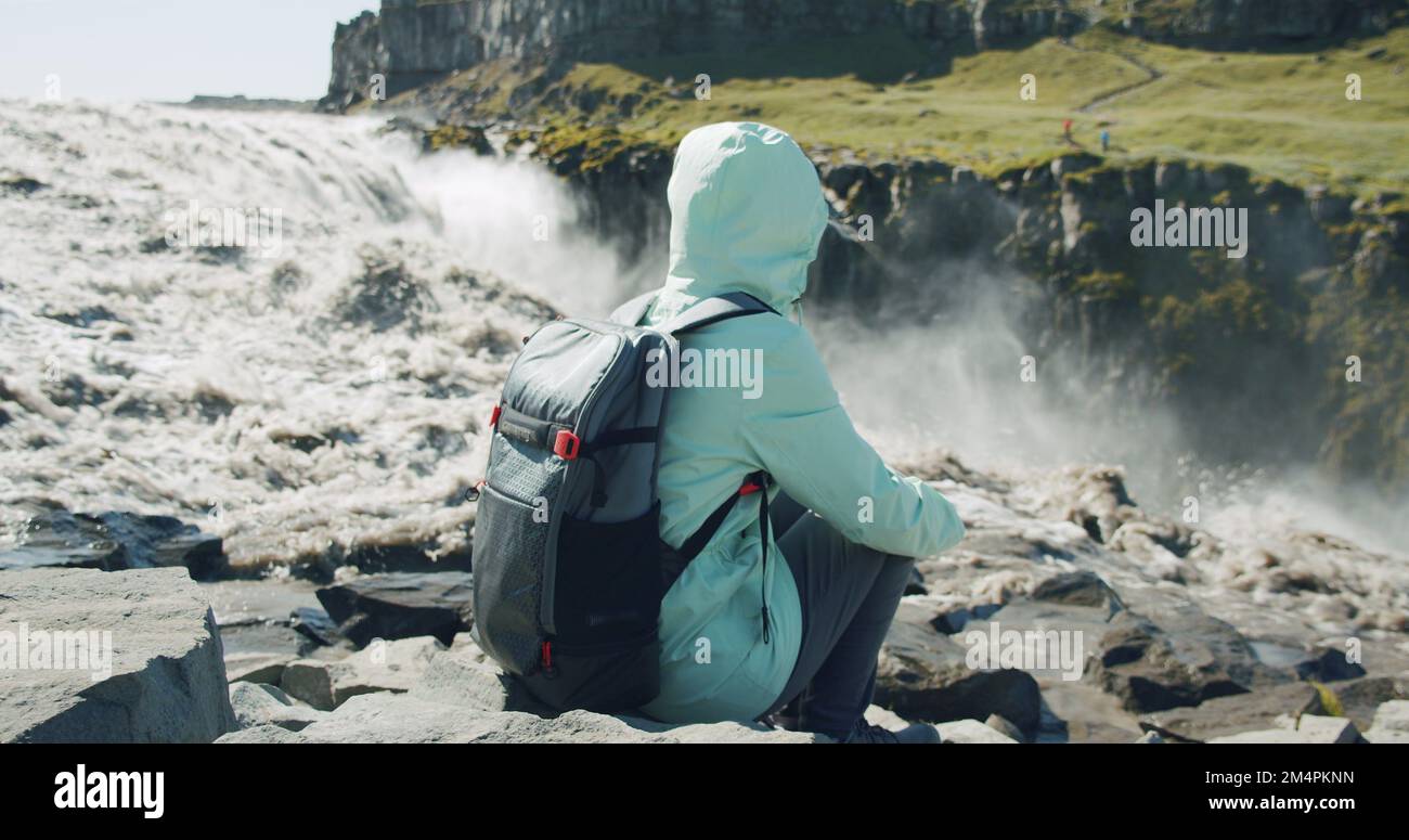 Woman sitting at cliff edge Defocused running river falling into ...