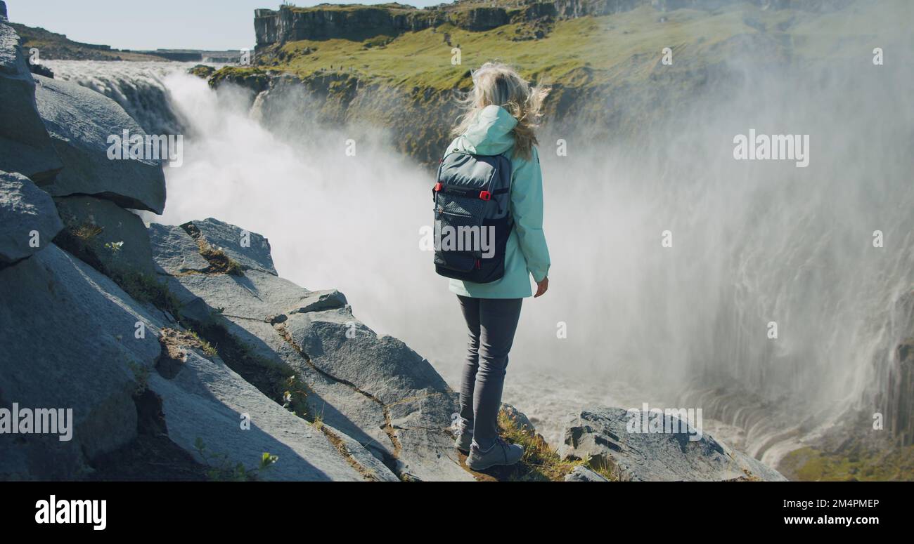 Woman standing at cliff edge looking at powerful Detifoss waterfall in ...