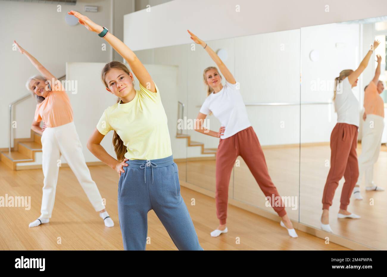Teen girl with family doing aerobics exercises with group of people in ...