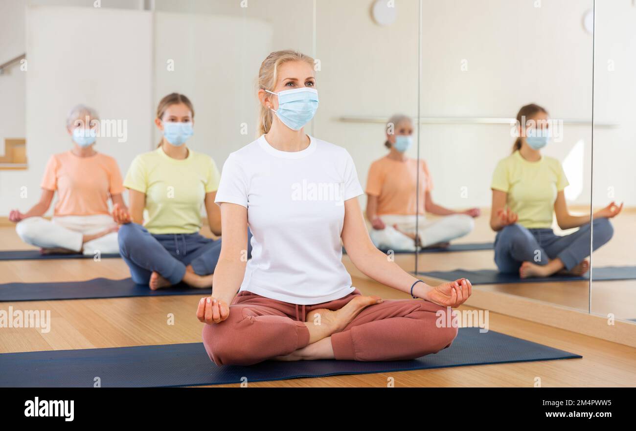 Group of people in protective mask sitting in lotus position practicing ...