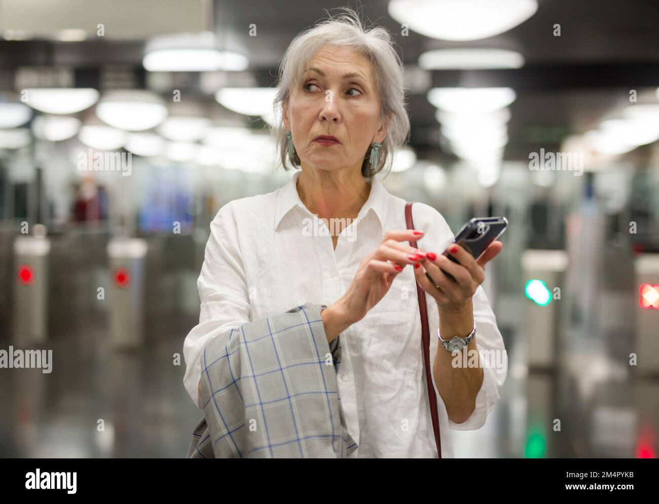 Lady standing and uisng smartphone near ticket barriers Stock Photo - Alamy