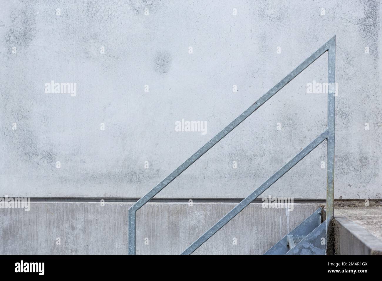 The grey stair railing in front of an equally grey, weathered wall has ...