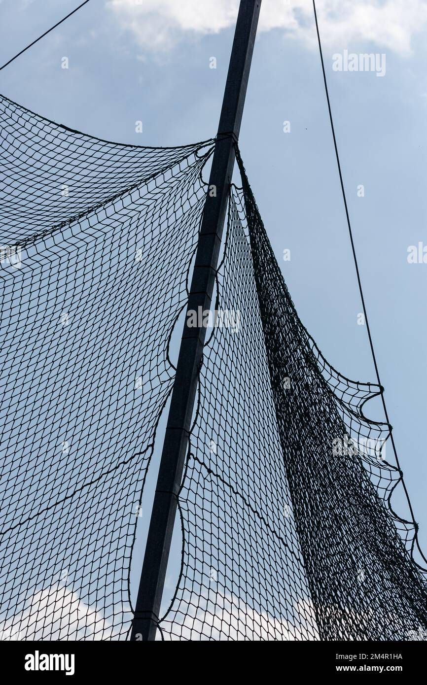 A rough net is tied to a pole against a blue sky with white clouds ...