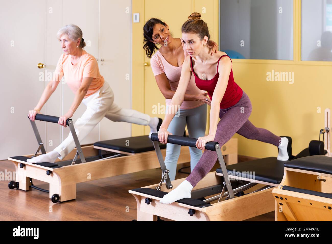 Hispanic female pilates instructor helping girl exercising on reformer ...