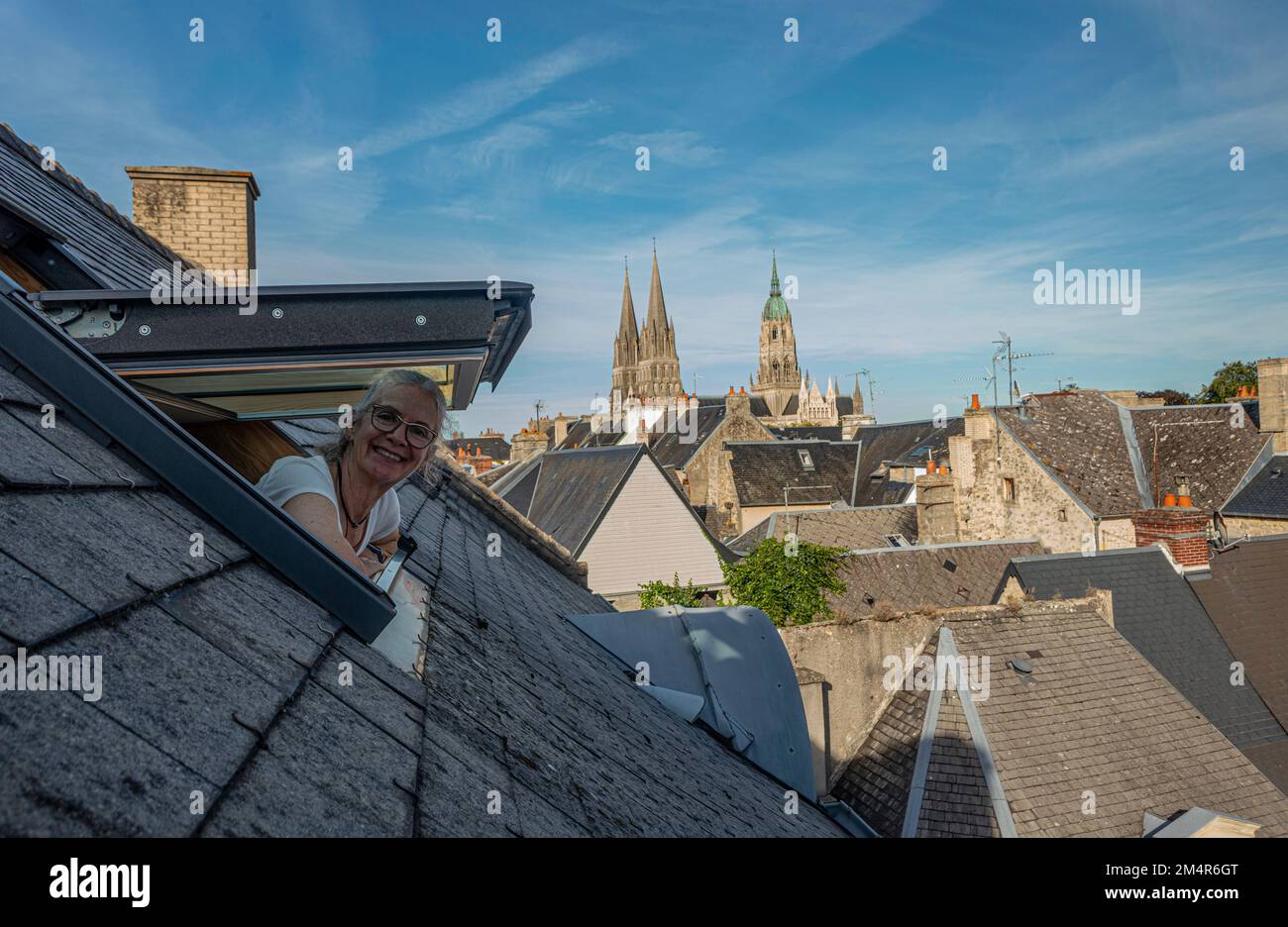 Woman looking out of skylight with skyline of Bayeaux, France in ...