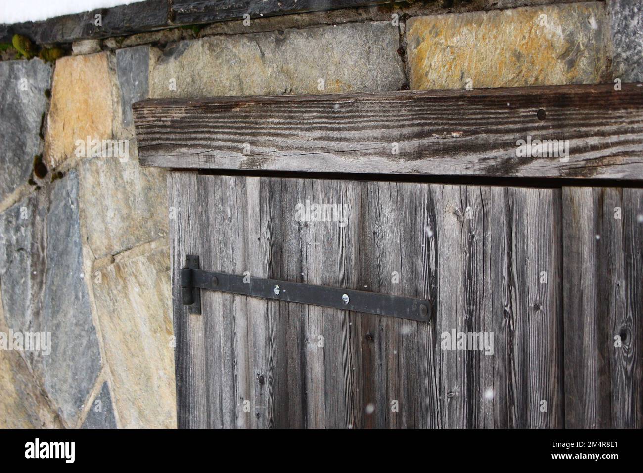 Snow falling in front of rustic wooden door outside set into a stone ...