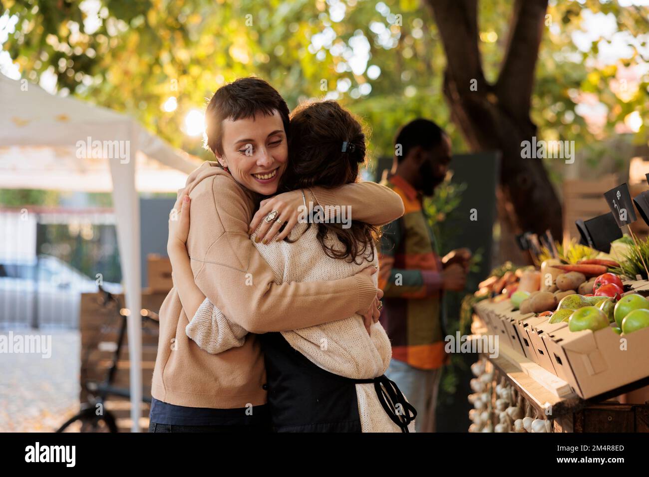 Friendly farmers market vendor hugging with happy female customer while ...