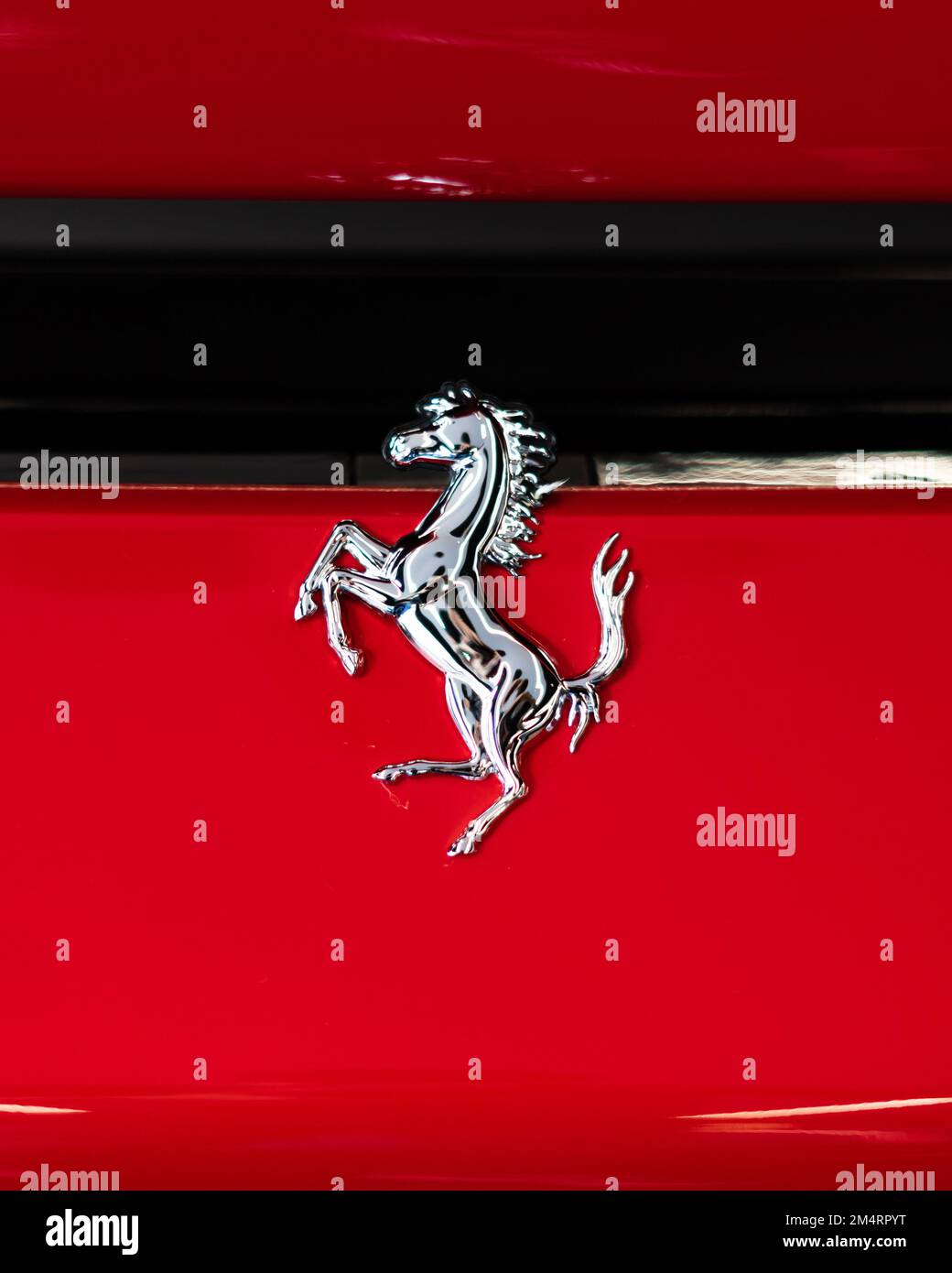 A vertical closeup shot of a Ferrari chrome horse badge, on a shiny red ...