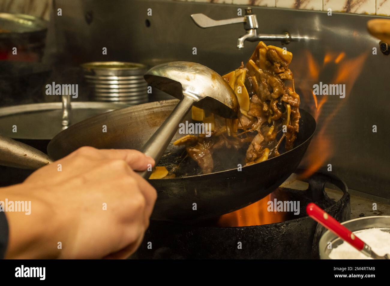An asian chef stir frying beef with mushrooms with a saucepan and wok ...