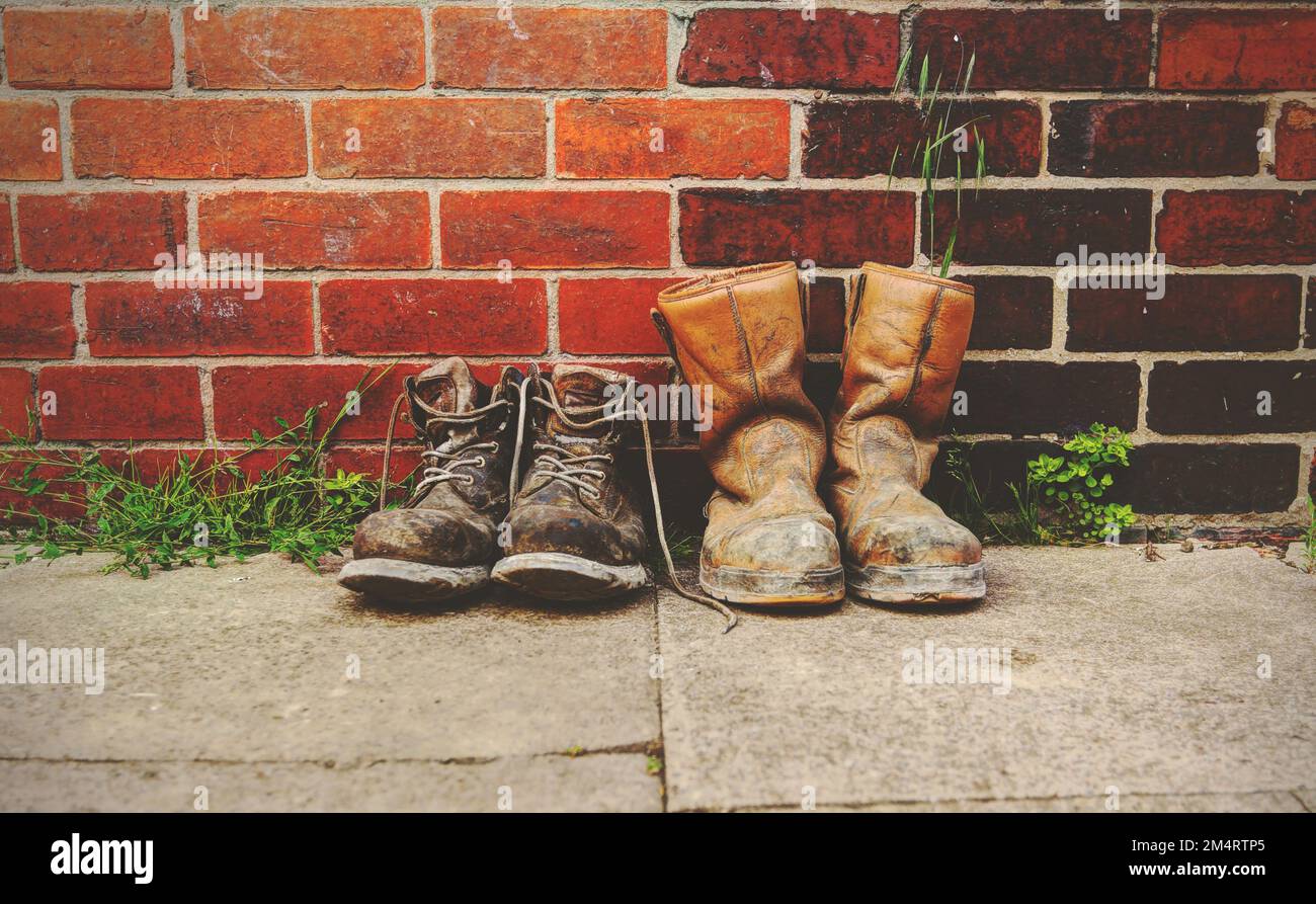 Two pairs of old boots in front of a brick wall.The boots are heavily ...
