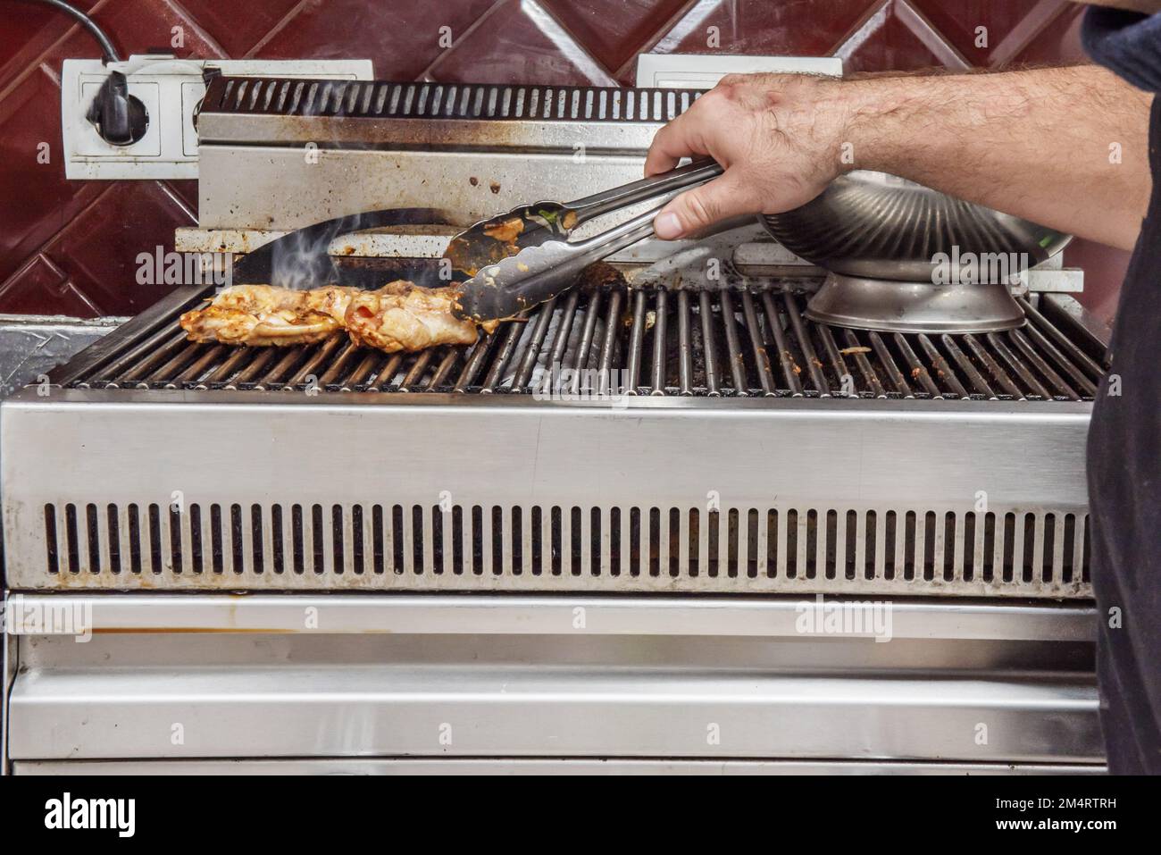 A kebab employee flipping chicken wings on a dirty electric grill Stock ...