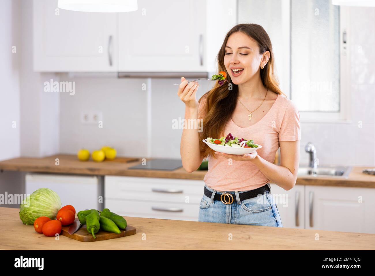 Cheerful woman eating vegetable salad at kitchen Stock Photo - Alamy