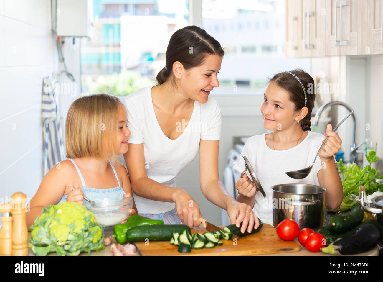 Young woman and two daughters cooking together Stock Photo - Alamy