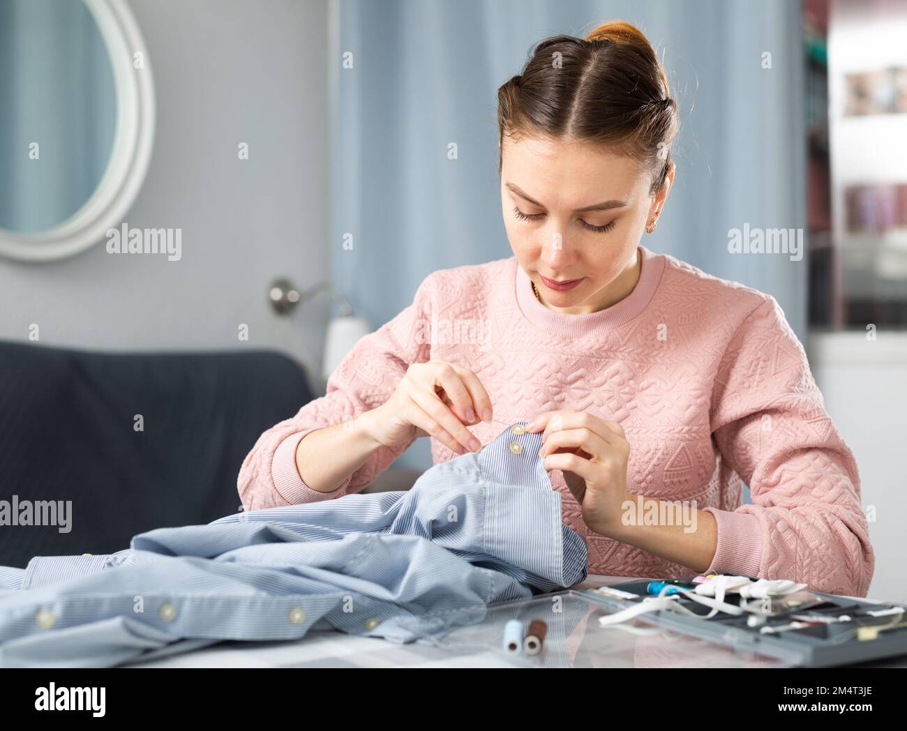 Woman repairing clothes with a needle and thread Stock Photo - Alamy