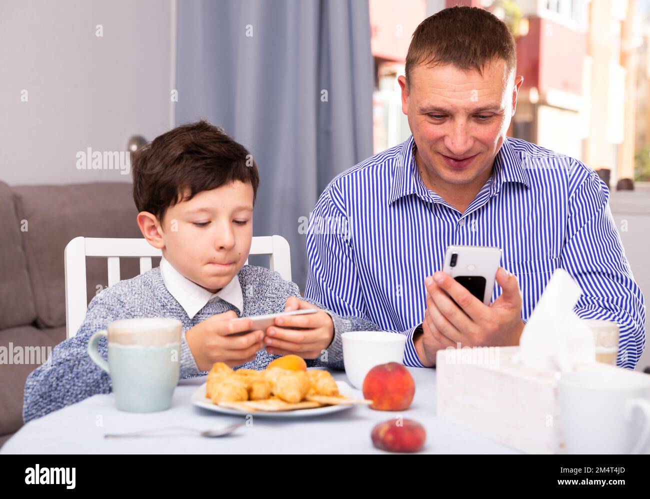 Young man and his son using phones at table with tea indoors Stock ...