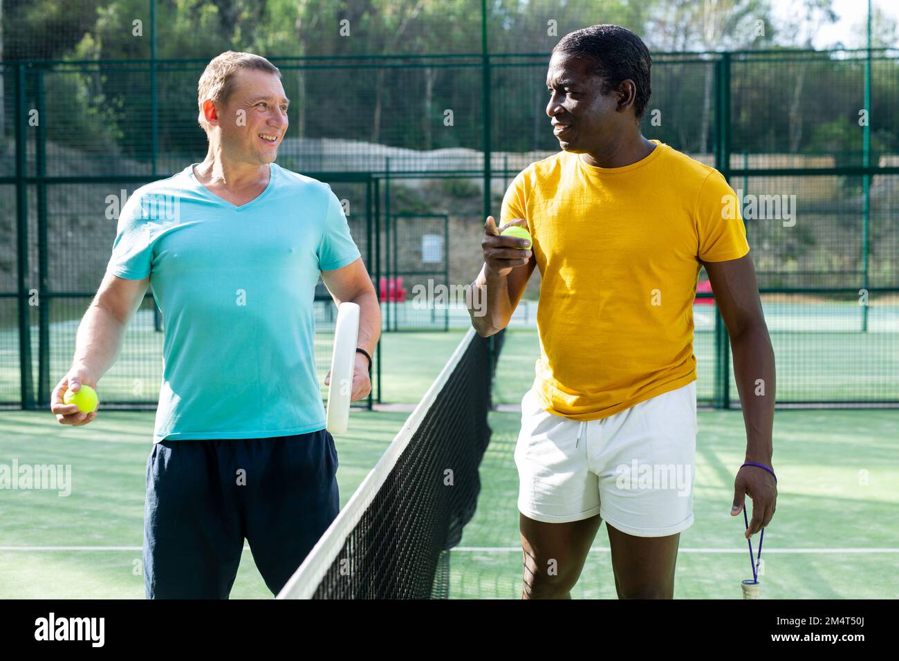 Two men padel tennis players on an outdoor court discussing something ...