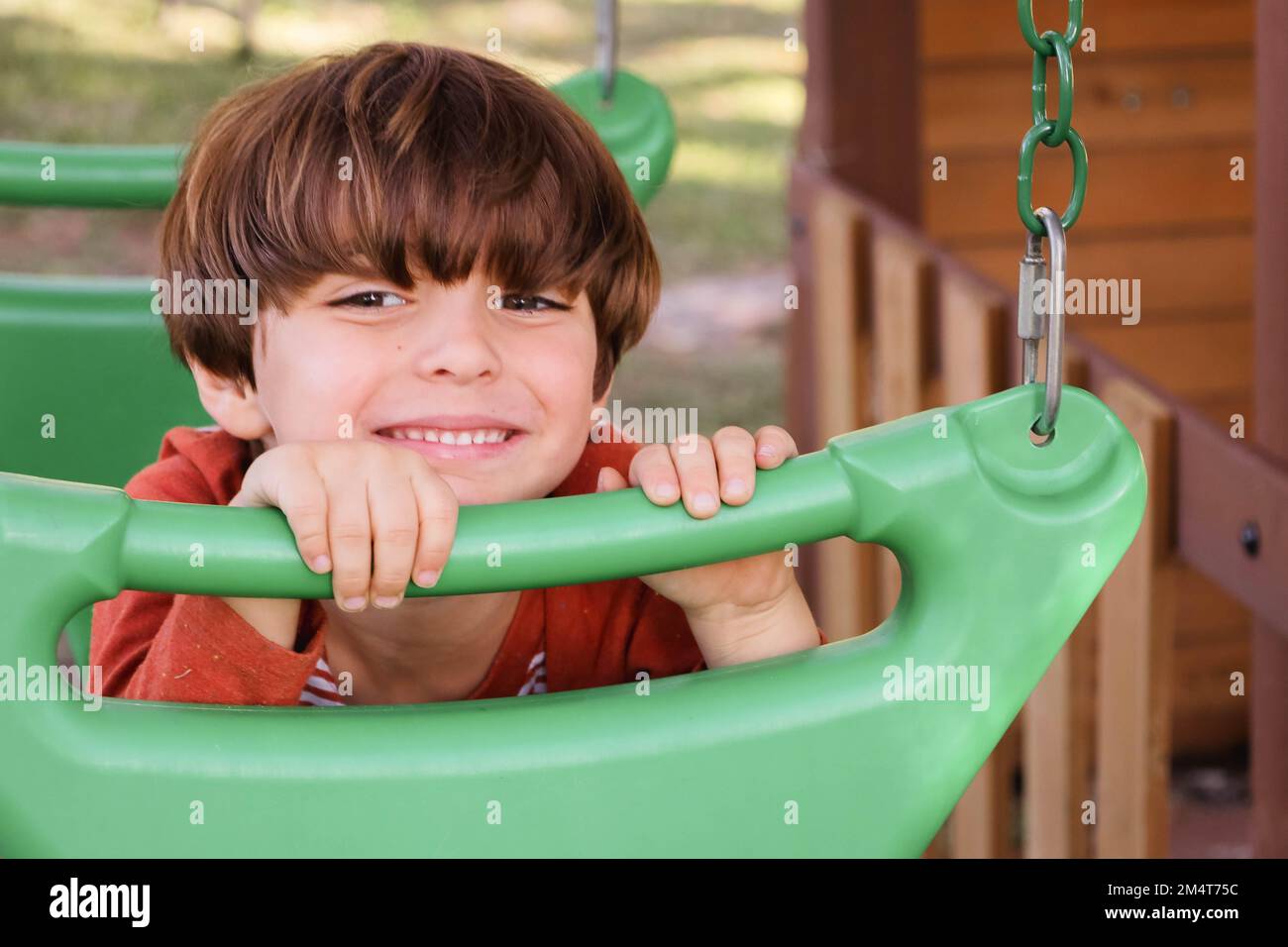 A portrait of a cute caucasian little boy leaning on the green swimg on ...