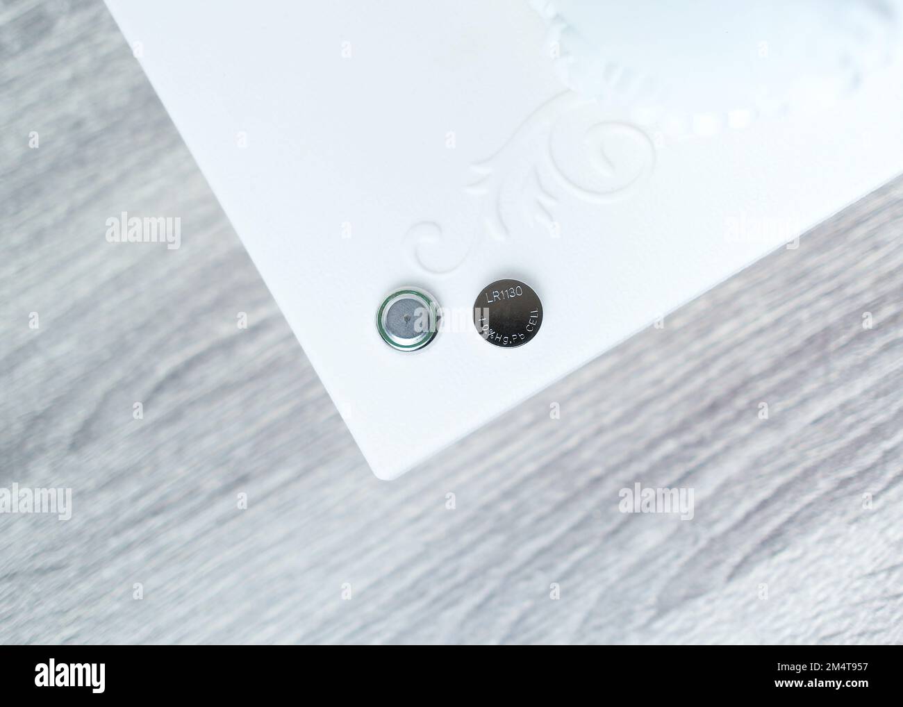 The front and back of the LR1130 coin or button cell battery sits on a ...