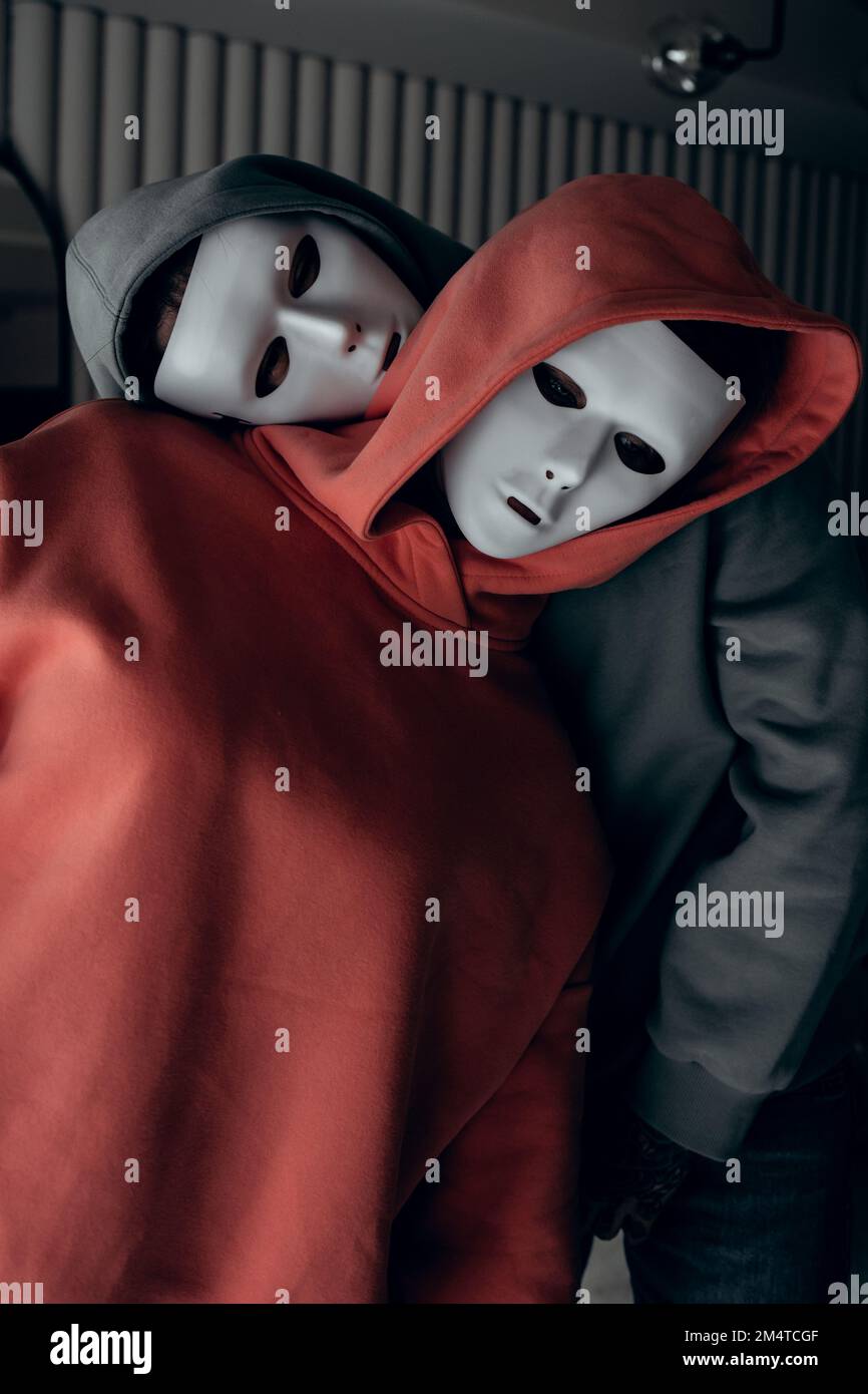 Portrait of two people in white theatrical masks and hood on black ...