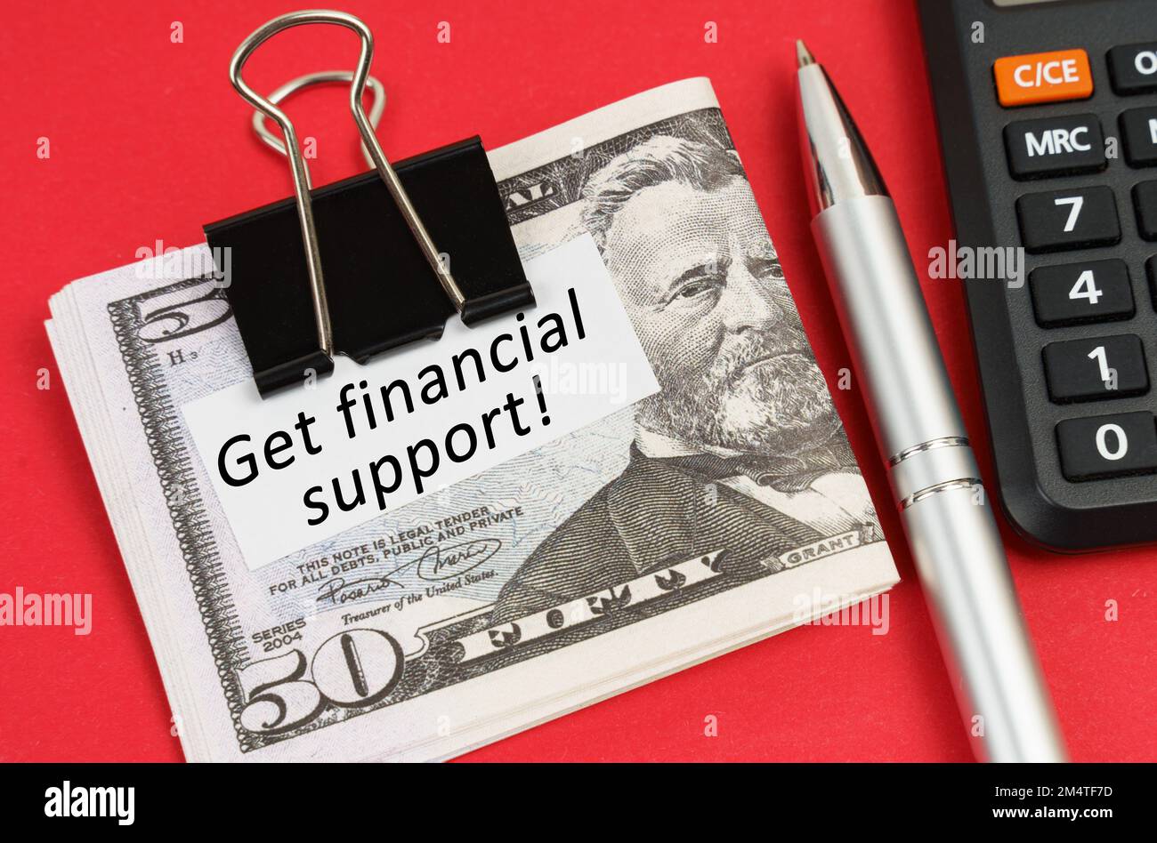 Business and economy concept. On a red surface lies a calculator, a pen, dollars. Dollars are ...