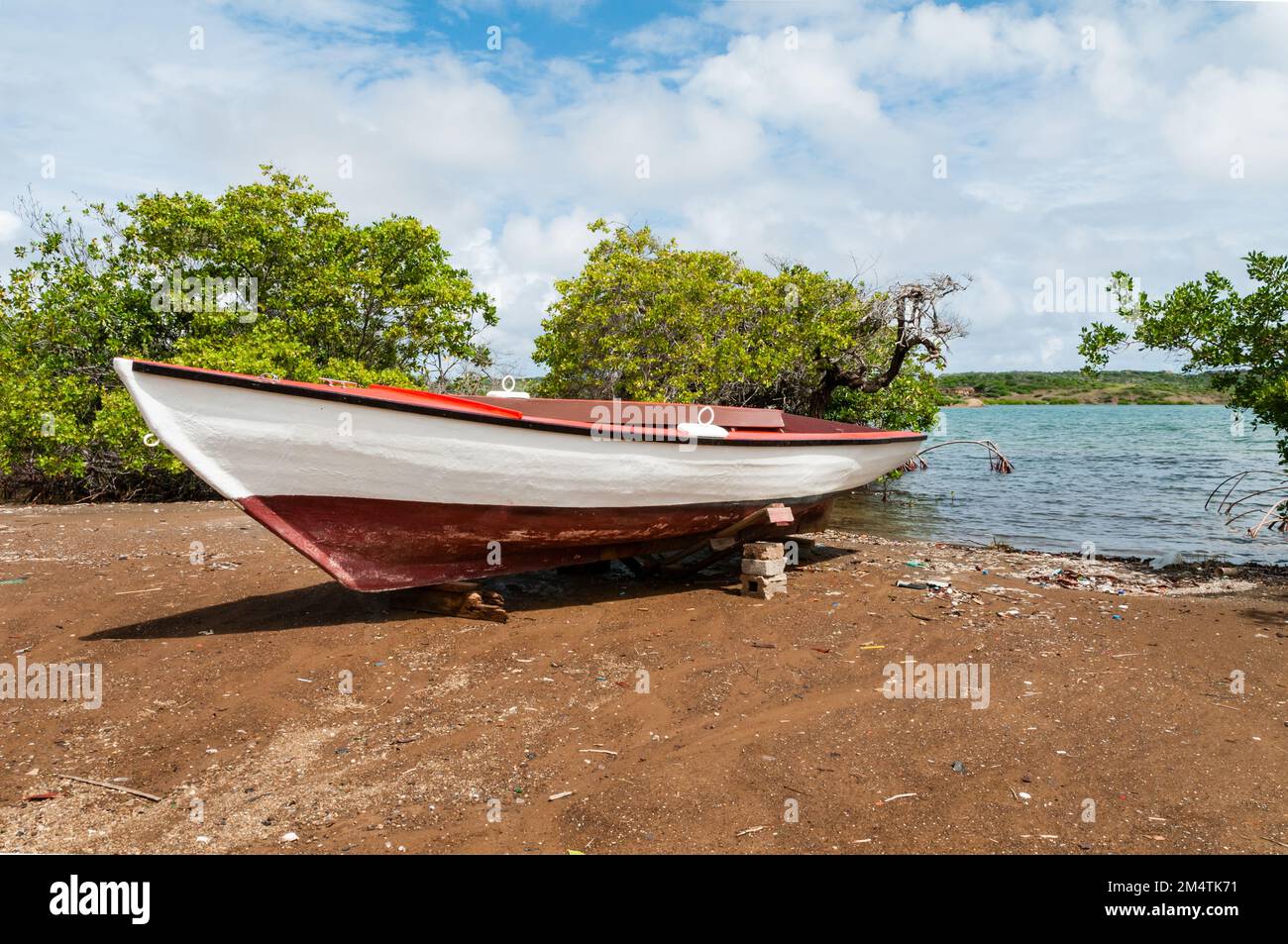 A white red painted boat lies on dry part of the beach of St. Joris Bay ...