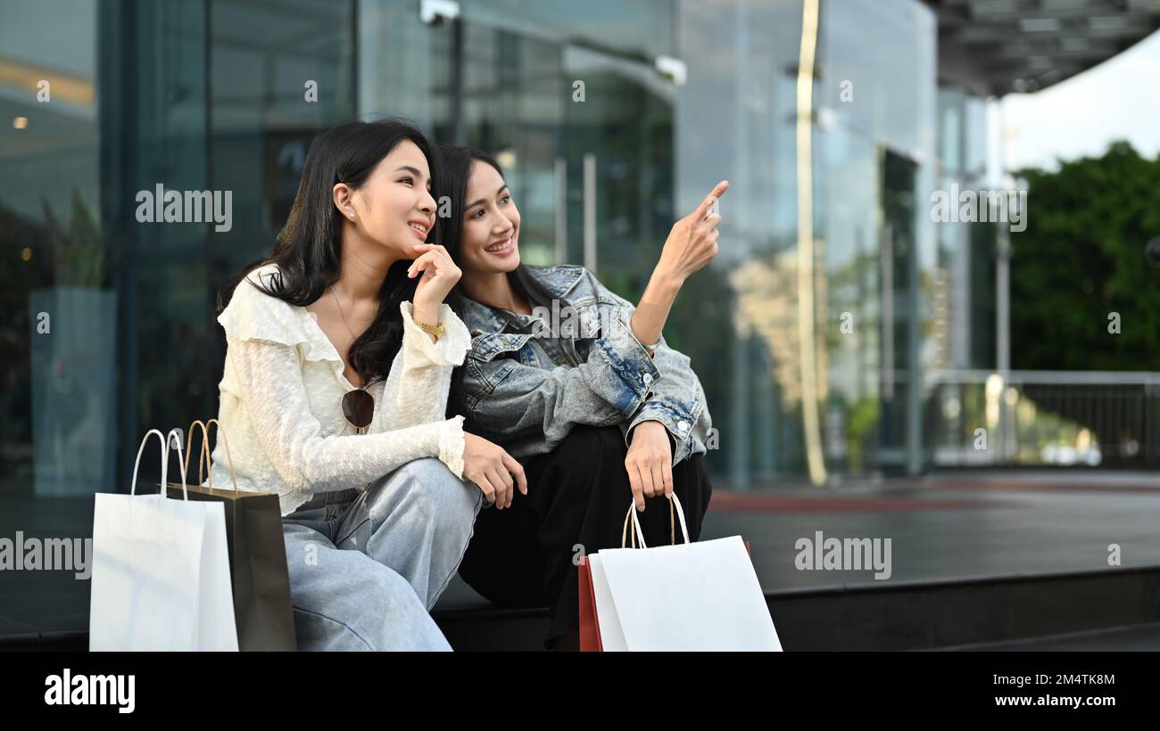 Two young Asian woman sitting at urban stairs with shopping bags and talking to etch other Stock ...