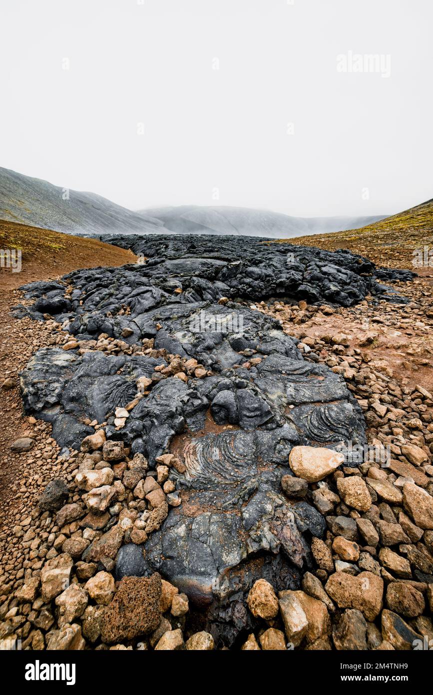 Vertical photo of cooled lava river stoping somewhere in the red soil ...