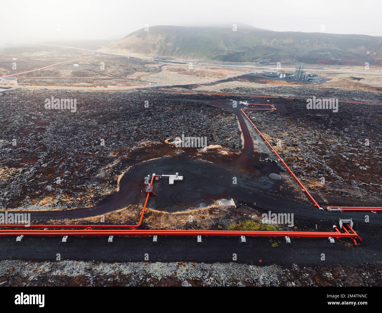 Aerial view of red pipes running on the black volcanic grounds in ...