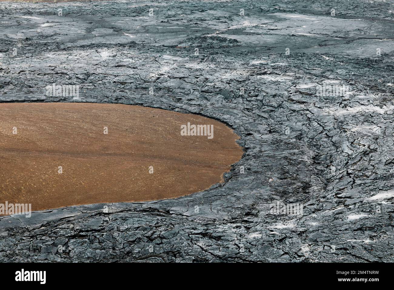 Cooled lava rocks surrounding a patch of red soil near Geldingadalir ...
