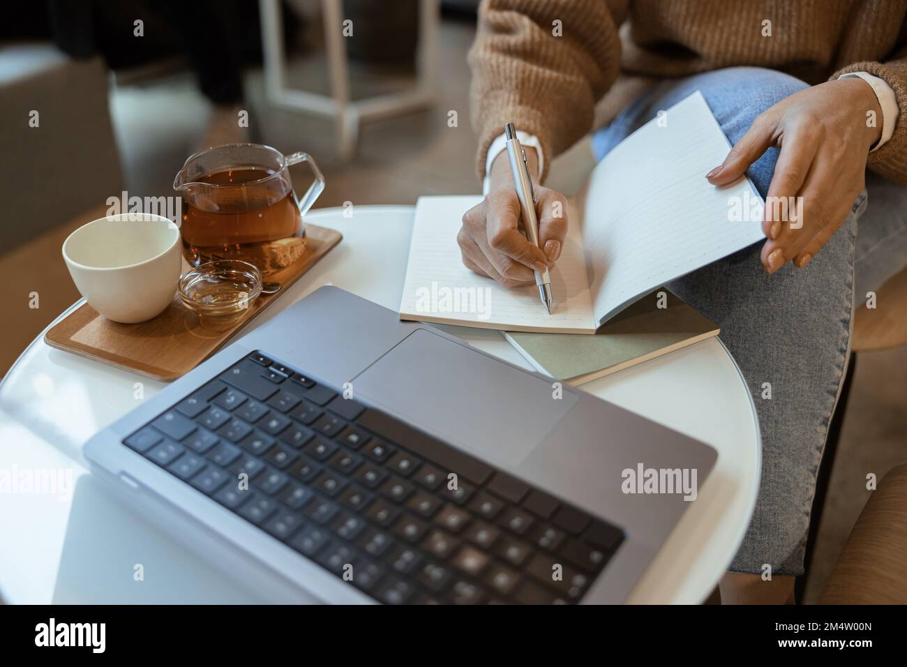 Close up of woman making notes in notepad while working laptop in cafe ...