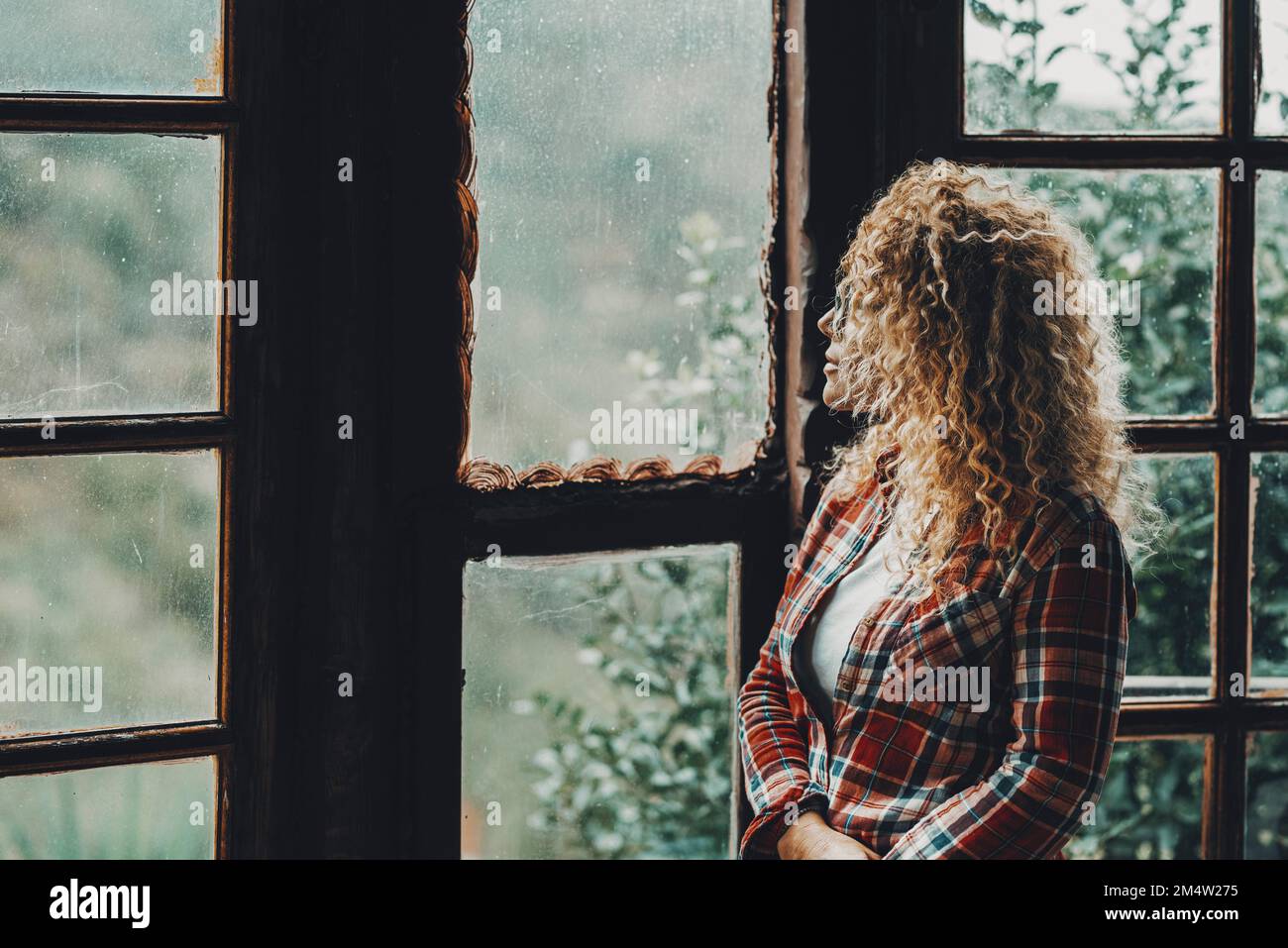 One woman standing alone at home looking outside the windows at nature ...