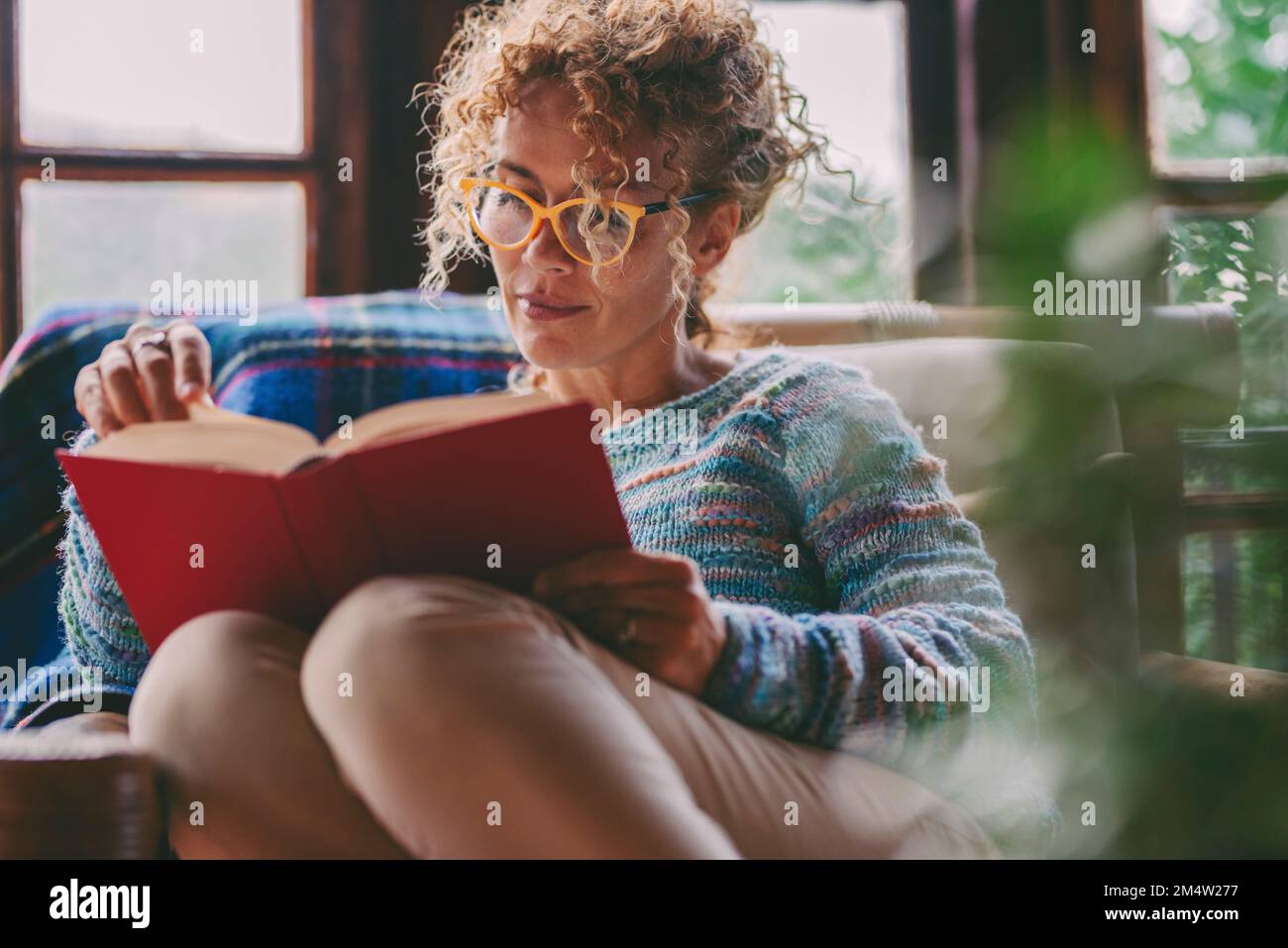 Woman at home sitting and reading a book in relax indoor leisure ...