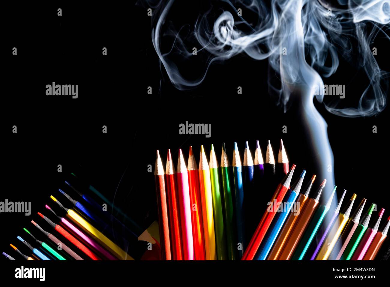 A closeup of colorful pencils and white smoke on a black background ...